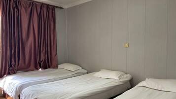 Quarto com duas camas de solteiro, janela com cortinas e interruptor na parede.