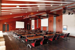 Sala de conferências com várias mesas, cadeiras, tela de projetor e quadro branco.