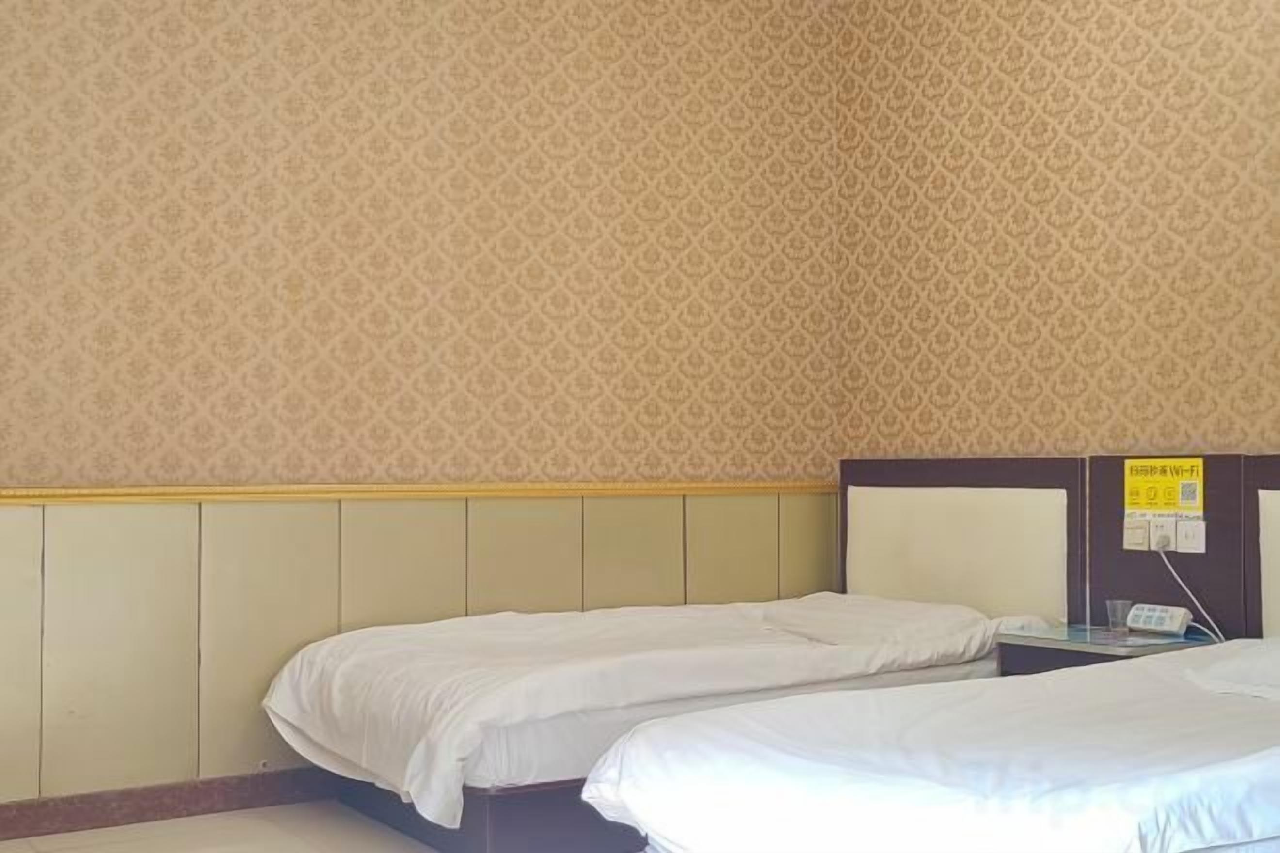 Quarto de hotel com duas camas, cabeceira e parede com papel de parede estampado.