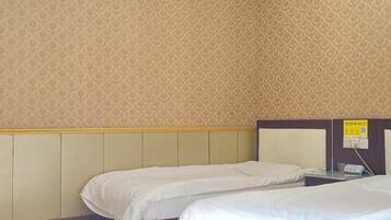 Quarto de hotel com duas camas, cabeceira e parede com papel de parede estampado.