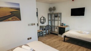 Quarto de hotel com duas camas, uma escrivaninha, uma cadeira, um guarda-roupa, uma televisão e um quadro de uma paisagem.