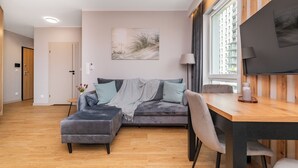 Uma sala de estar moderna com um sofá cinzento, uma mesa de jantar de madeira e uma grande janela com vista para um edifício.