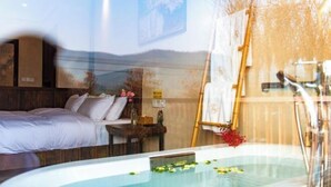 Quarto com cama, uma mesinha com um vaso e uma banheira com flores.