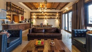 Uma sala de estar acolhedora com teto de madeira, sofás de couro, uma mesa de centro de madeira com frutas e um espaço de bar com prateleiras e garrafas.