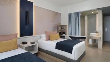 Quarto de hotel moderno com duas camas, uma escrivaninha, toucador com espelho e área de chuveiro.