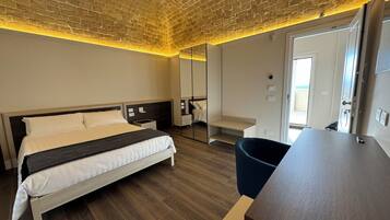 Quarto de hotel moderno com uma cama grande, uma escrivaninha, uma cadeira e um espelho.