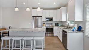 Uma cozinha moderna com armários brancos, eletrodomésticos de aço inoxidável e uma ilha de mármore com banquetas.