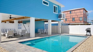 Uma piscina com área de estar coberta, mobiliário de exterior e um salão de piscina cercado.