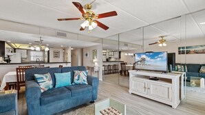 Uma sala de estar moderna com um sofá azul, uma televisão e um ventilador de teto.