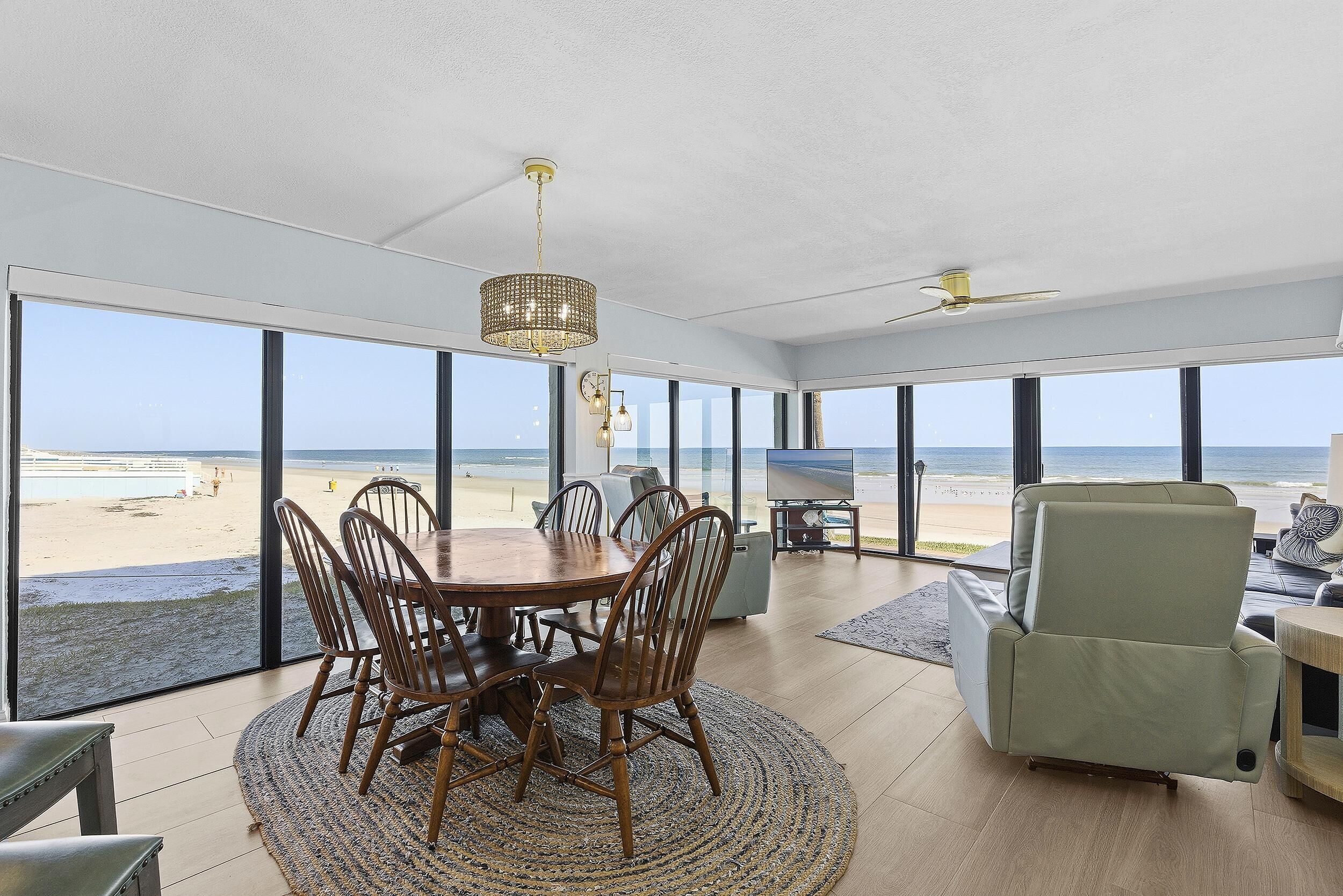 Um quarto amplo com uma mesa de jantar, cadeiras e vista para a praia.