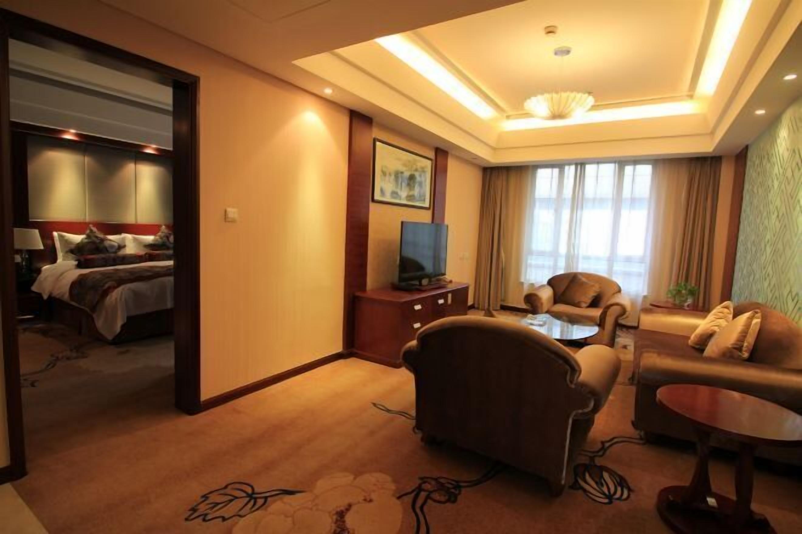 Quarto de hotel com uma cama, um sofá, uma mesa de centro, uma televisão e uma janela grande.