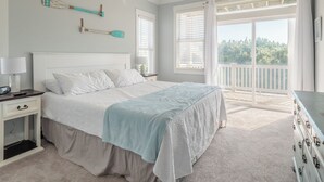 Quarto com cama, mesas de cabeceira, cômoda, ventilador de teto e varanda com vista.