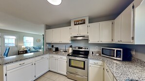 Cozinha moderna com armários brancos, bancada de granito, eletrodomésticos de aço inoxidável e uma placa com a inscrição 'hey yall'.