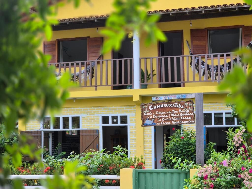 Um edifício de dois andares com varanda, rodeado por vegetação exuberante e flores.