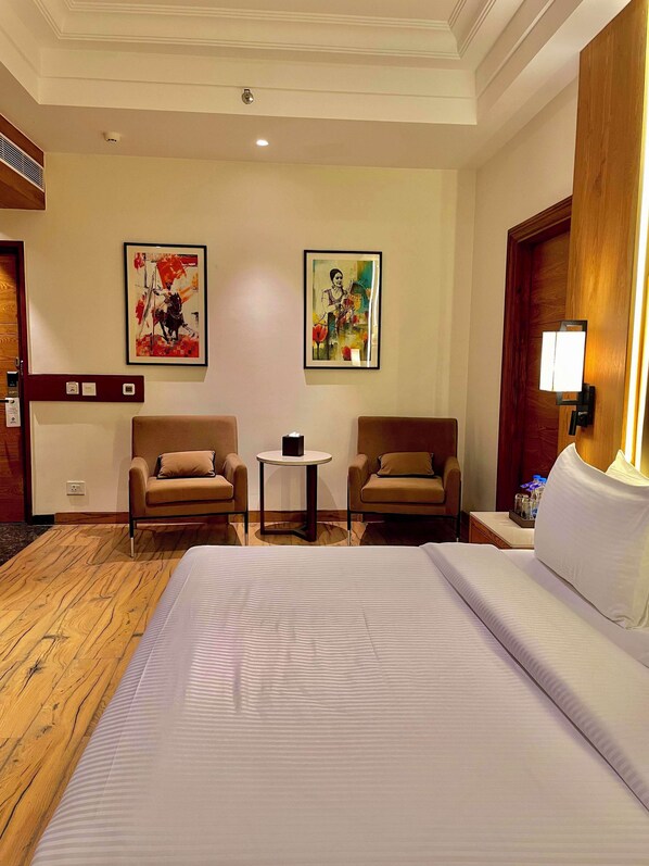 Quarto de hotel com uma cama grande, duas poltronas, uma mesinha e duas pinturas na parede.