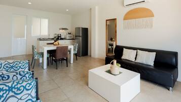 Uma sala de estar moderna com um sofá preto, uma mesa de centro branca e cadeiras estampadas.