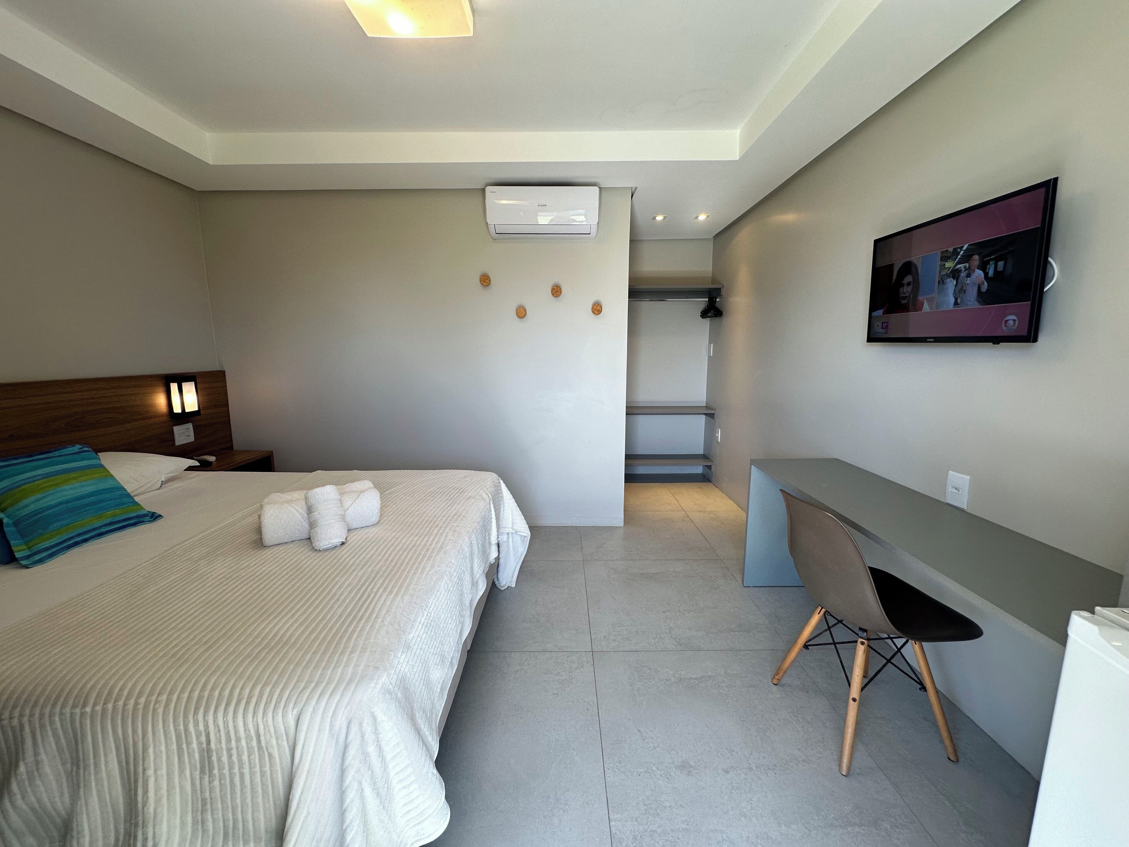 Quarto de hotel com cama, escrivaninha, cadeira, ar condicionado e televisão.