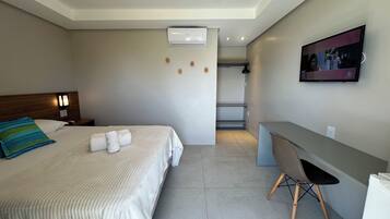 Quarto de hotel com cama, escrivaninha, cadeira, ar condicionado e televisão.