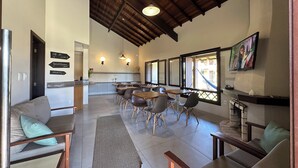 Uma sala de jantar espaçosa com tetos altos e vigas de madeira, com mesas e cadeiras dispostas para refeições.