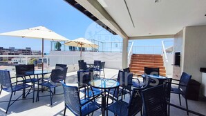 Terraço no terraço com área de estar externa, incluindo mesas e cadeiras, e um grande guarda-sol para proteção contra o sol.