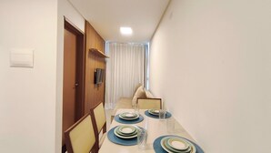 Um corredor com uma mesa de jantar posta para quatro, uma televisão presa a um painel de madeira e uma janela com cortinas.