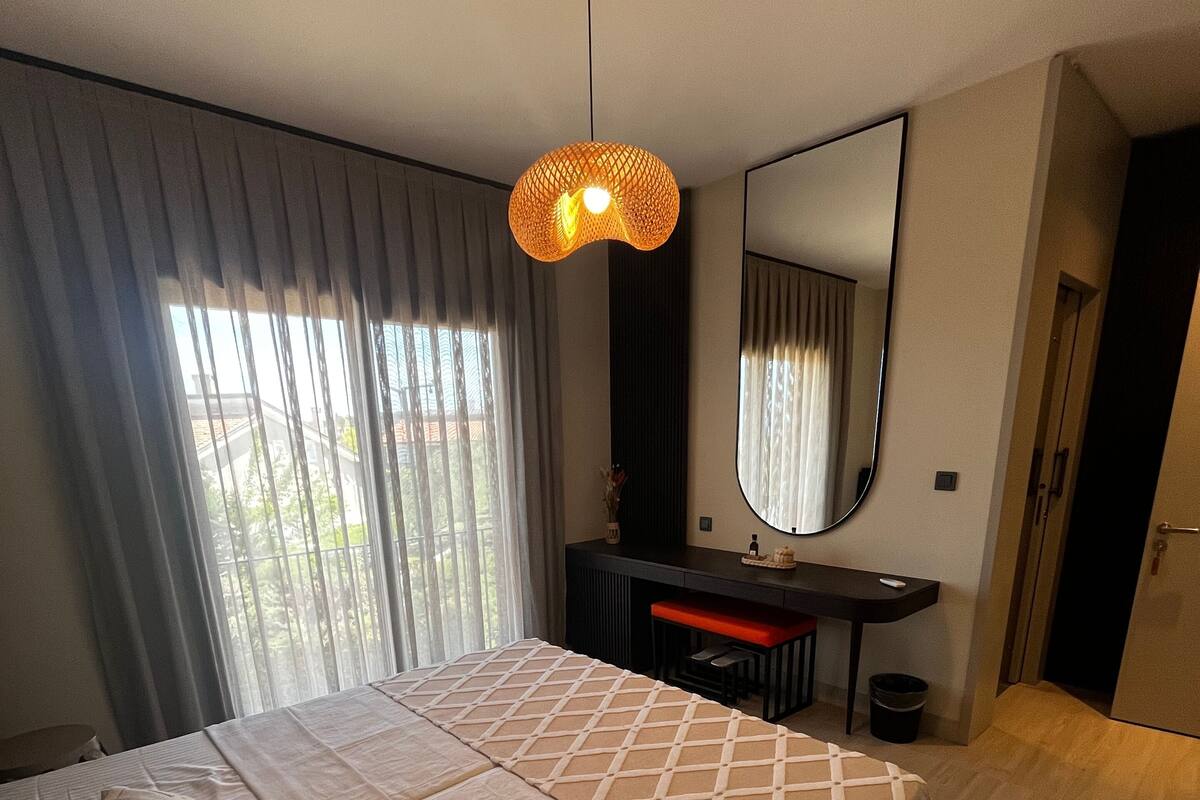 Quarto com cama, escrivaninha, espelho e luminária suspensa.