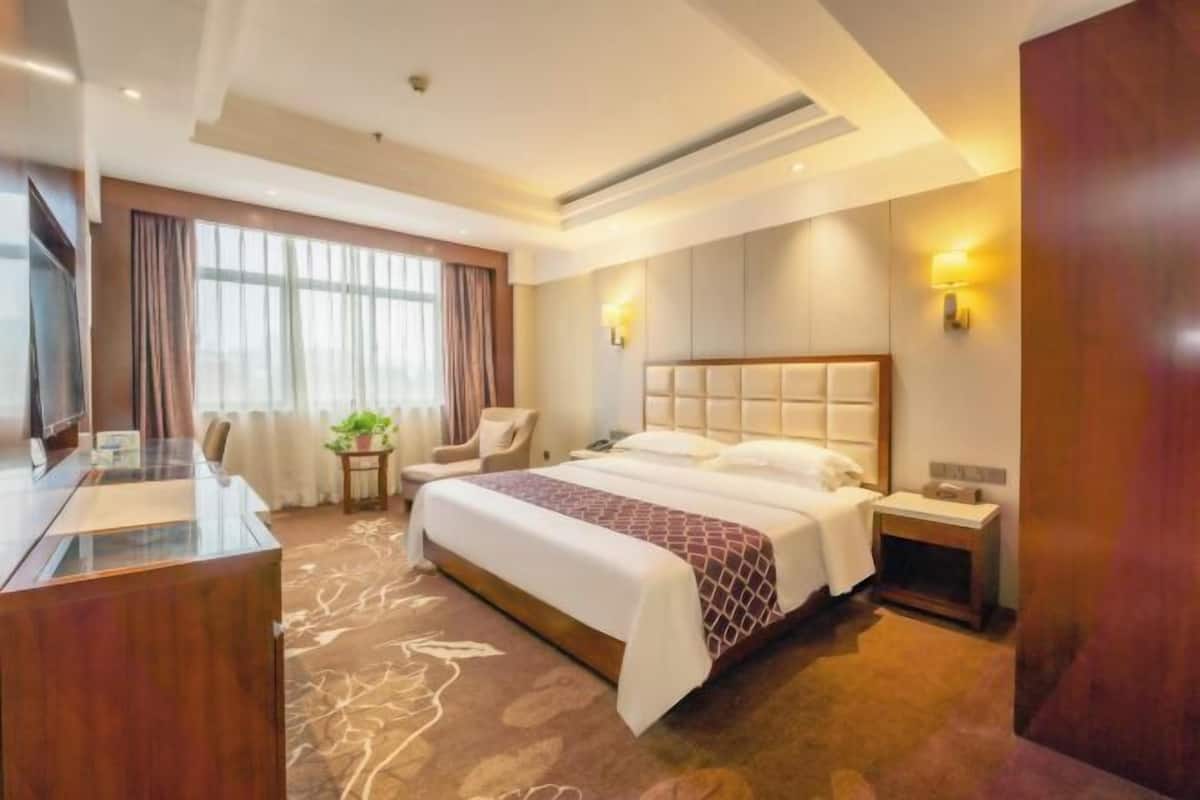 Quarto de hotel com uma cama grande, uma escrivaninha, uma cadeira, televisão e janela com cortinas.