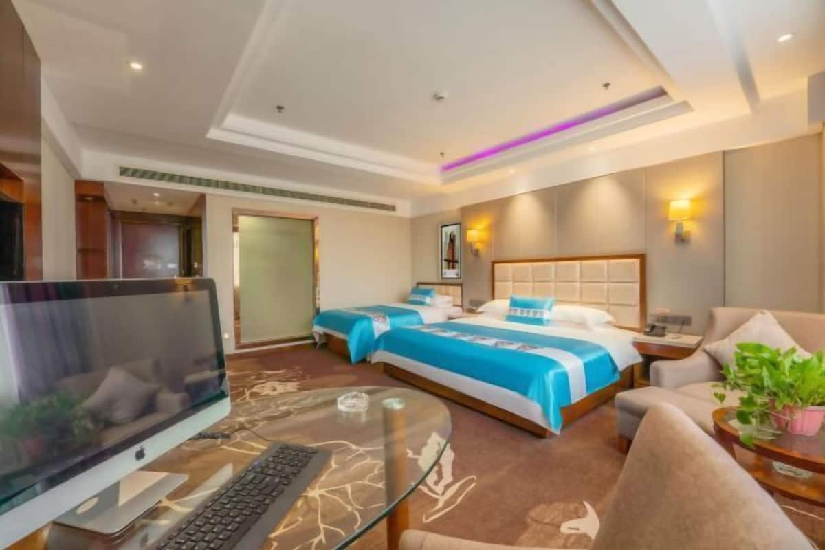 Quarto de hotel com duas camas, uma mesa de escritório com computador, uma TV e um sofá.