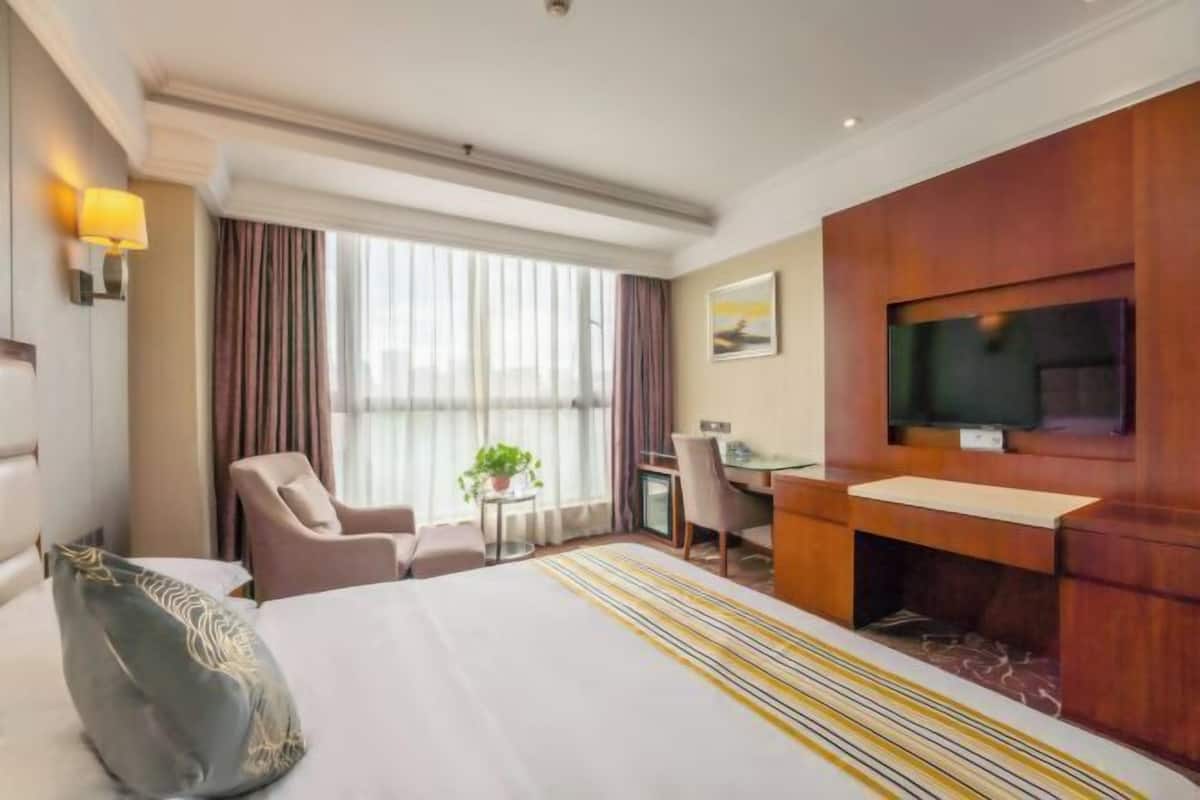 Quarto de hotel com cama, escrivaninha, cadeira, televisão e janela com cortinas.