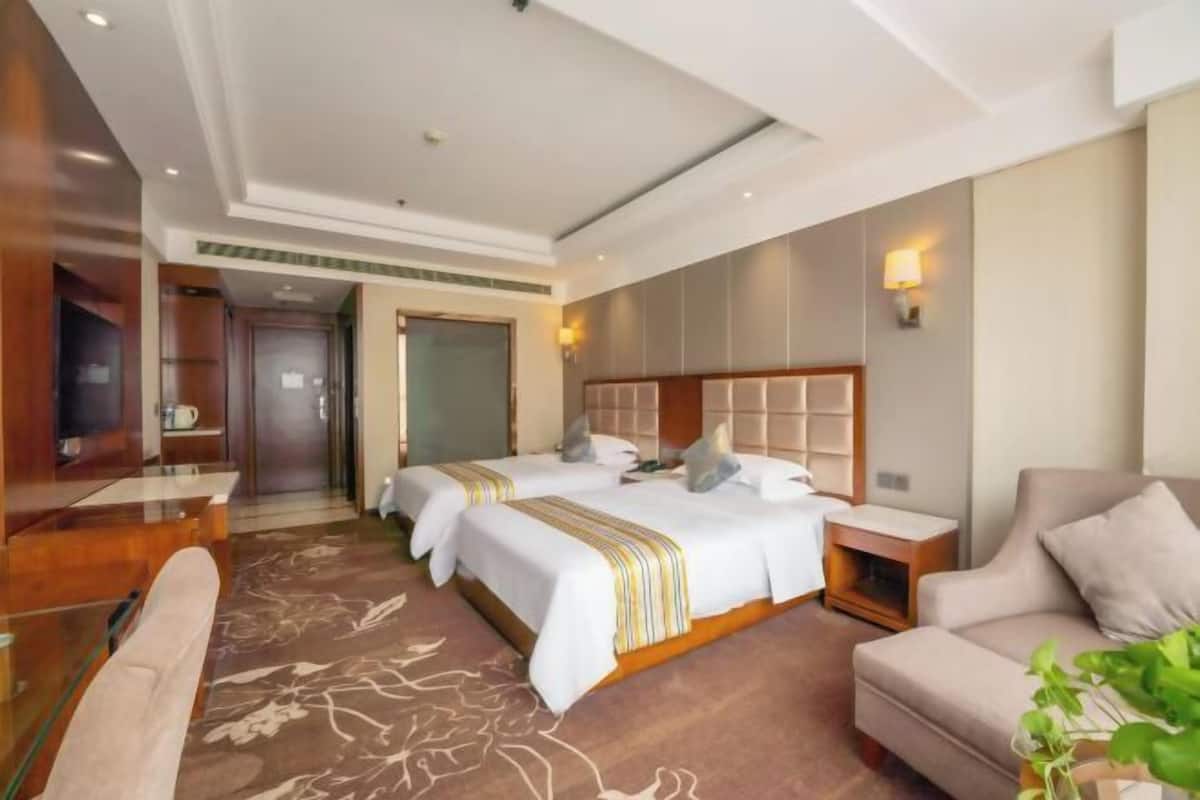 Quarto de hotel com duas camas, um sofá, uma mesinha e uma mesa de cabeceira.