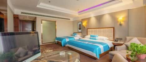 Quarto de hotel com duas camas, uma escrivaninha com computador, televisão e um sofá.