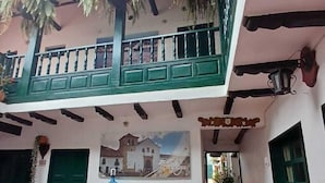 Um edifício de dois andares com uma varanda, uma mesa com toalha florida e uma cadeira.