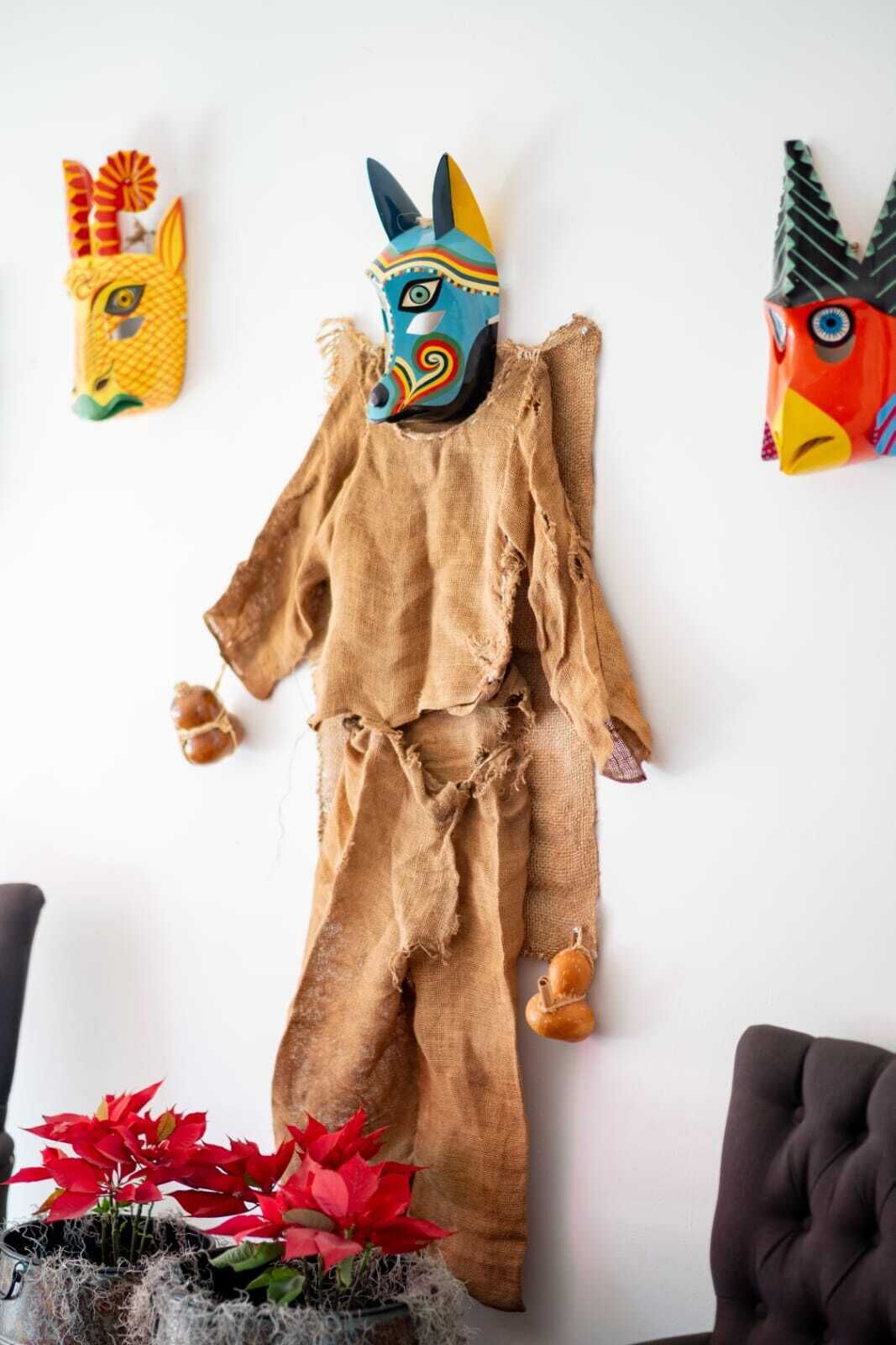Quarto com um adereço rústico de serapilheira pendurado na parede, cercado por máscaras coloridas.