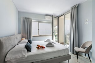 Quarto moderno com cama grande, uma cadeira, janela e vista para o exterior.