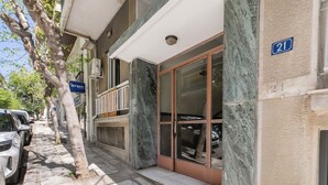 Um edifício com uma placa azul indicando o número 21, entrada com portão e carros estacionados ao longo da calçada.