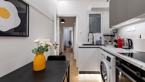 Cozinha moderna com máquina de lavar, área de refeições com um vaso amarelo e um corredor que leva a outro quarto.
