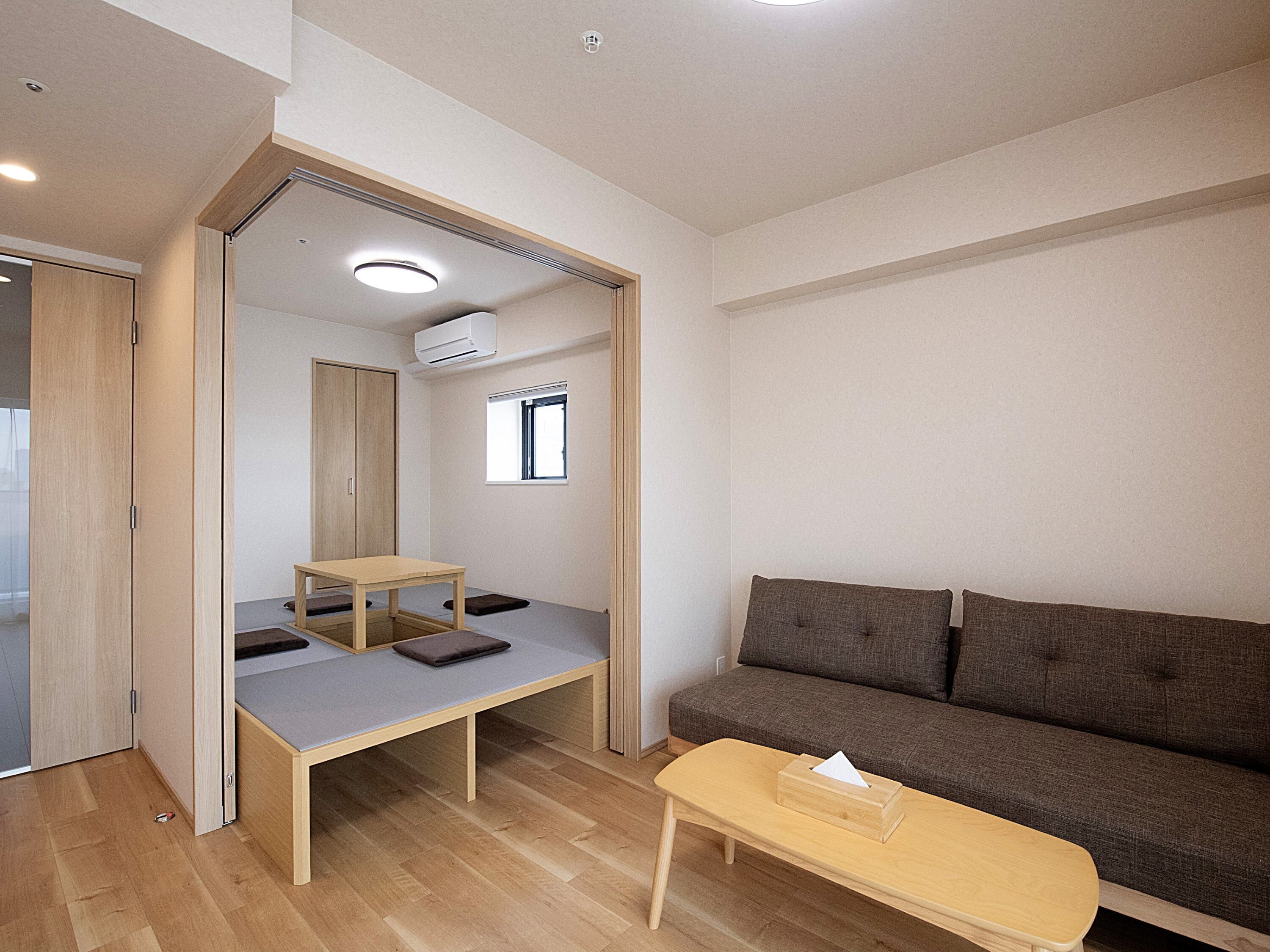 Um espaço compacto com sofá, mesa pequena, banco e porta deslizante que dá para outro ambiente.