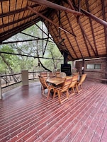 Um deck de madeira ao ar livre com telhado de palha, cercado por árvores.