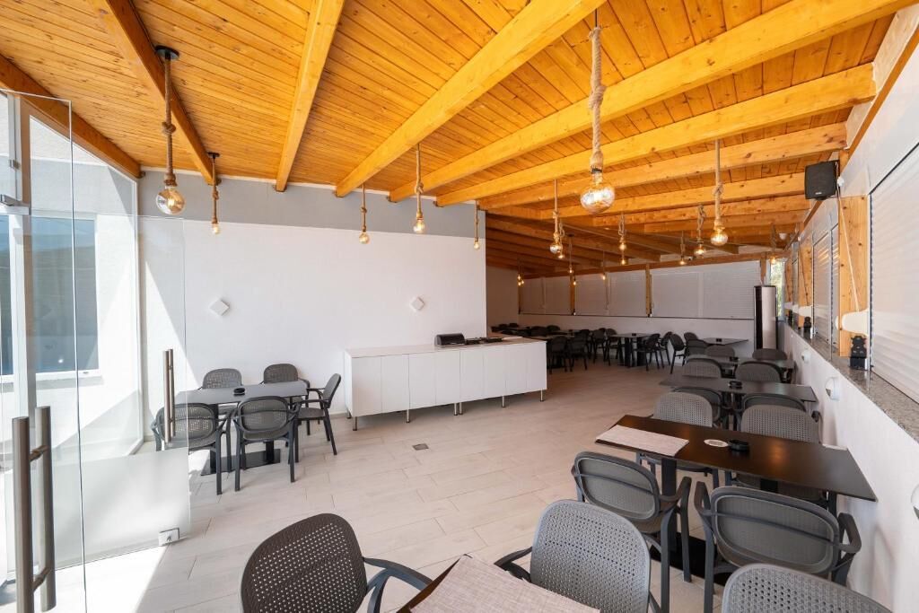 Uma sala de jantar ampla, com vigas de madeira no teto, mobiliário moderno e uma grande janela que proporciona iluminação natural.