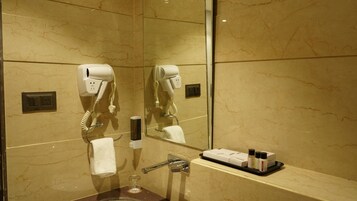 Uma casa de banho com parede de mármore, um porta-toalhas, um espelho, um secador de cabelo, uma pia e um tabuleiro com produtos de higiene pessoal.