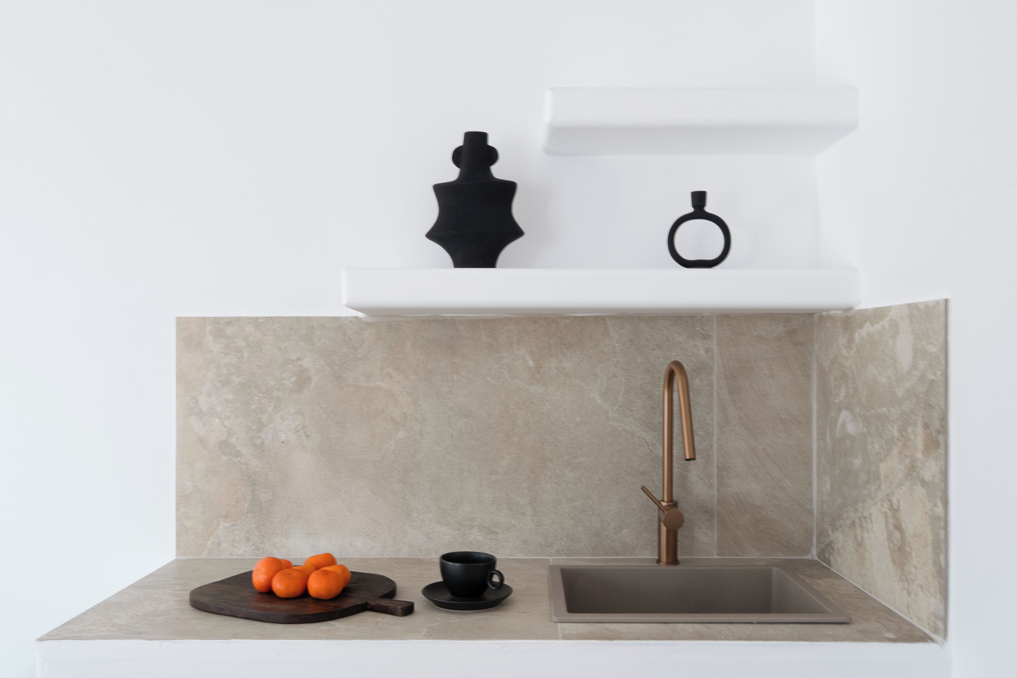 Uma cozinha com pia, bancada e prateleira com objetos decorativos.