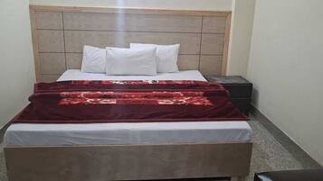 Uma cama com cabeceira de madeira, roupa de cama branca e um cobertor vermelho.