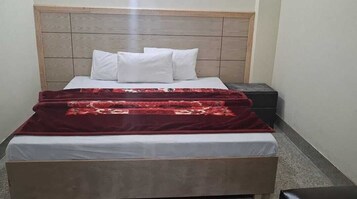 Uma cama com cabeceira de madeira, roupa de cama branca e um cobertor vermelho.