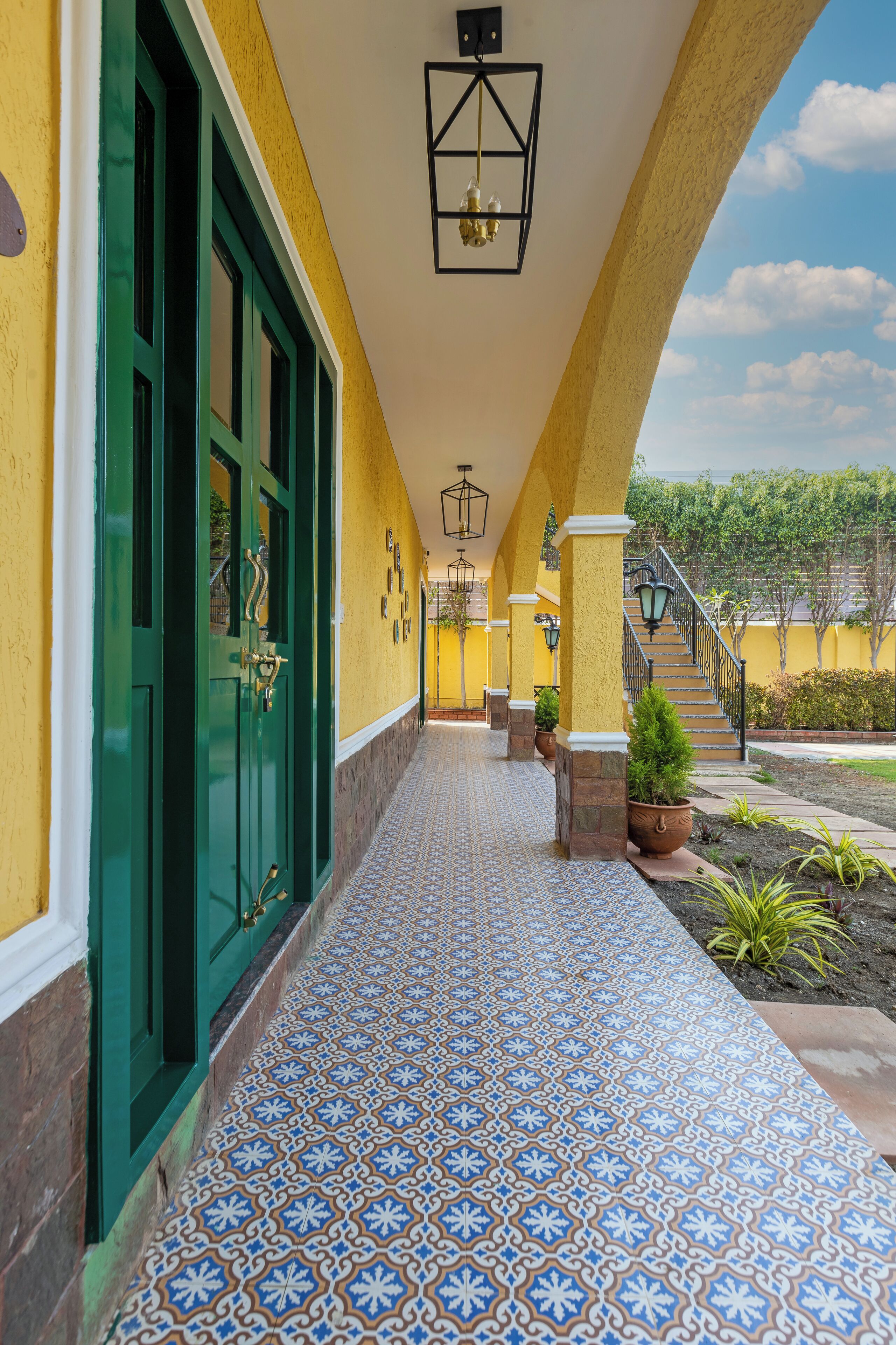 Corredor com ladrilhos estampados, portas verdes e escadaria que leva a um jardim.