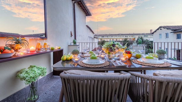 Mesa de jantar posta para uma refeição, vista para o pôr do sol, área de estar externa e guarda-corpo de varanda.