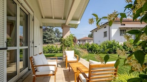 Um alpendre coberto com móveis de madeira e vista para um jardim bem cuidado e casas vizinhas.