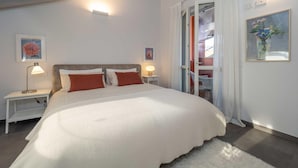 Um quarto com uma cama grande, duas mesas de cabeceira com luminárias, um tapete branco e um quadro na parede.