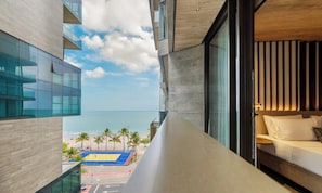 Quarto de hotel moderno com varanda vista para uma praia e quadra de tênis.
