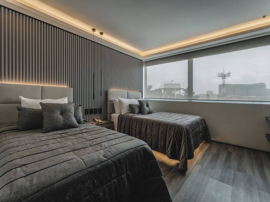 Quarto de hotel moderno com duas camas, uma janela grande e vista para a cidade.