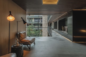 Interior moderno com um sofá de couro, uma luminária de chão e vista para um edifício com varanda.